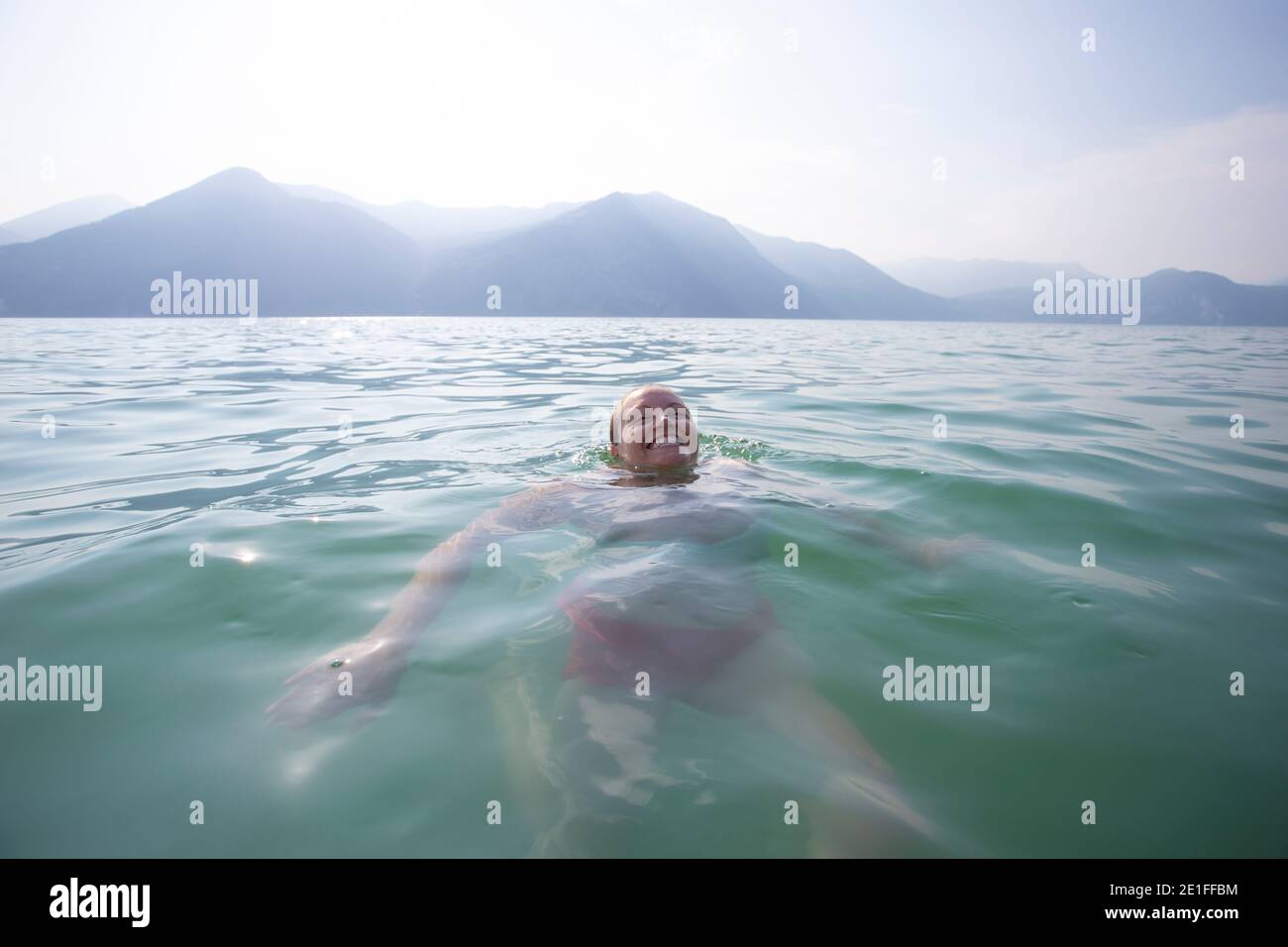 A smiling, floating woman in the middle of an alpine lake in Italy ...