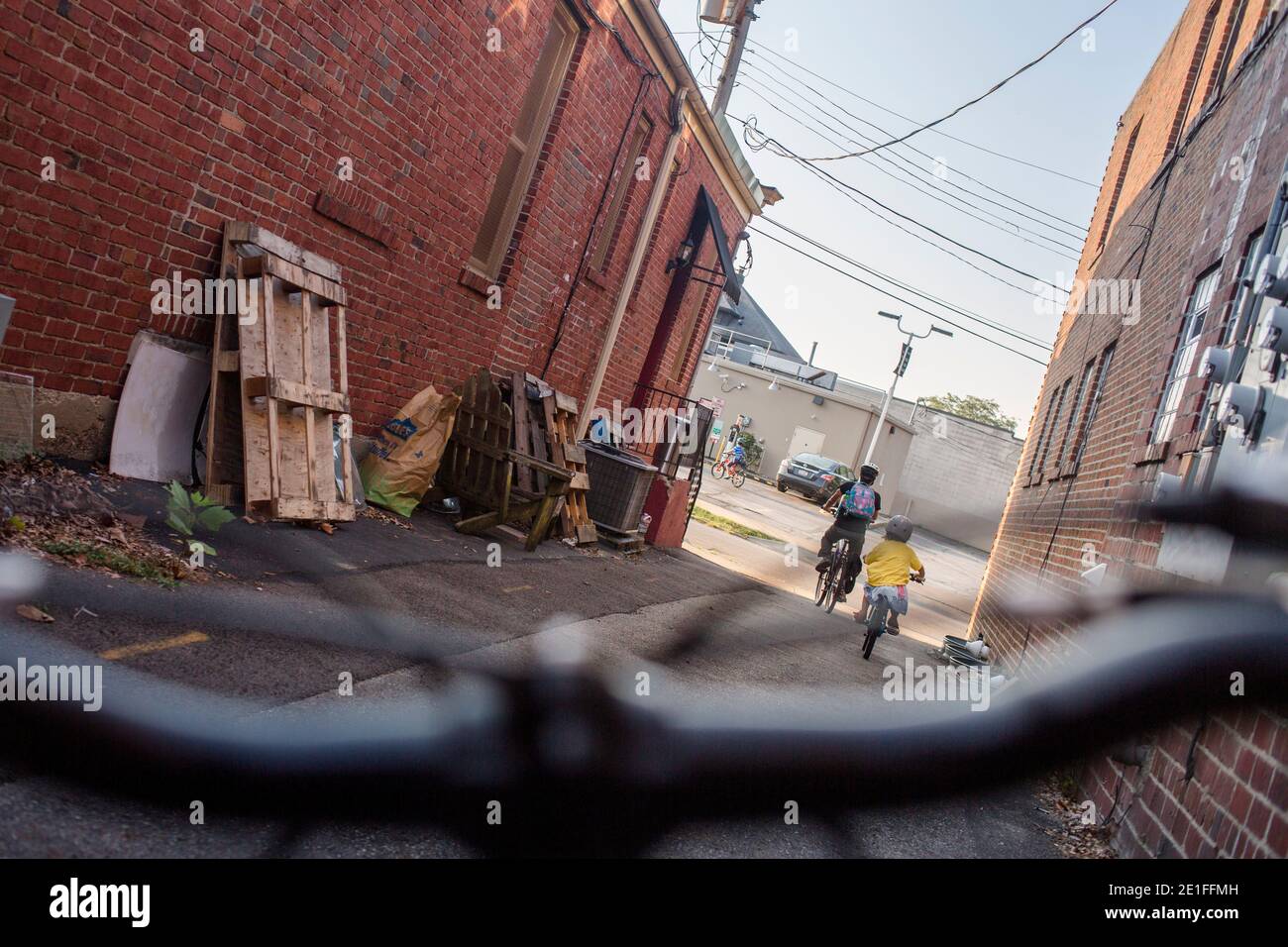 A family bikes to school together through a brick alleyway Stock Photo ...