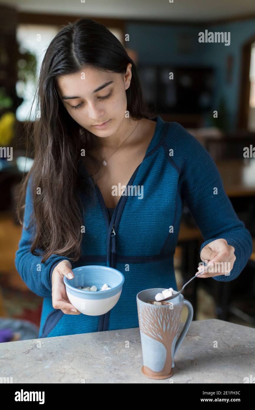pretty teen girl spooning marshmallows into hot cocoa in cozy interior ...