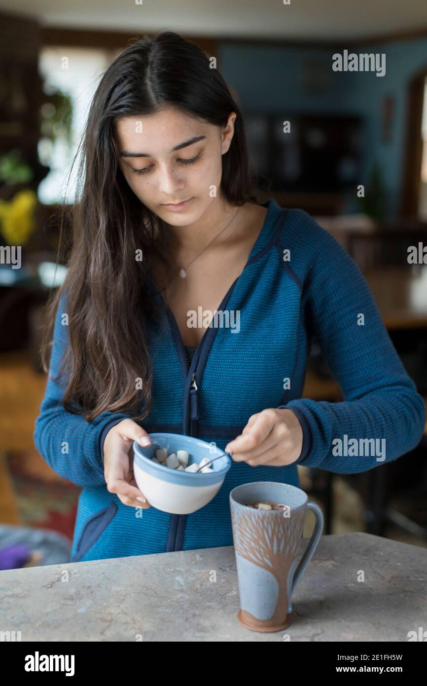 pretty teen girl spooning marshmellows into hot cocoa in cozy interior ...