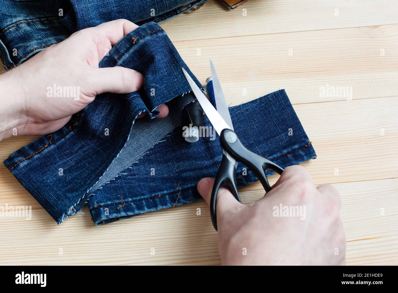 Tailor's hands with scissors cut denim. Wood background Stock Photo - Alamy