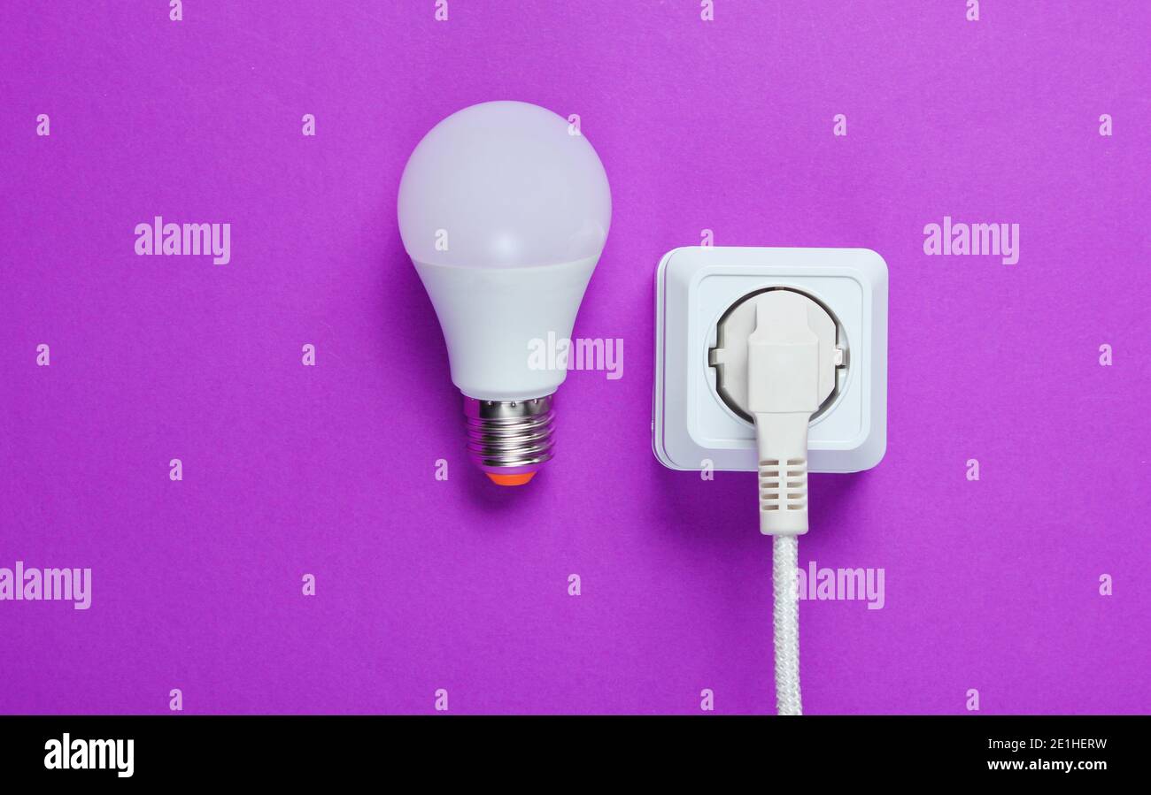 White cable plugged into power outlet and LED light bulb on purple ...