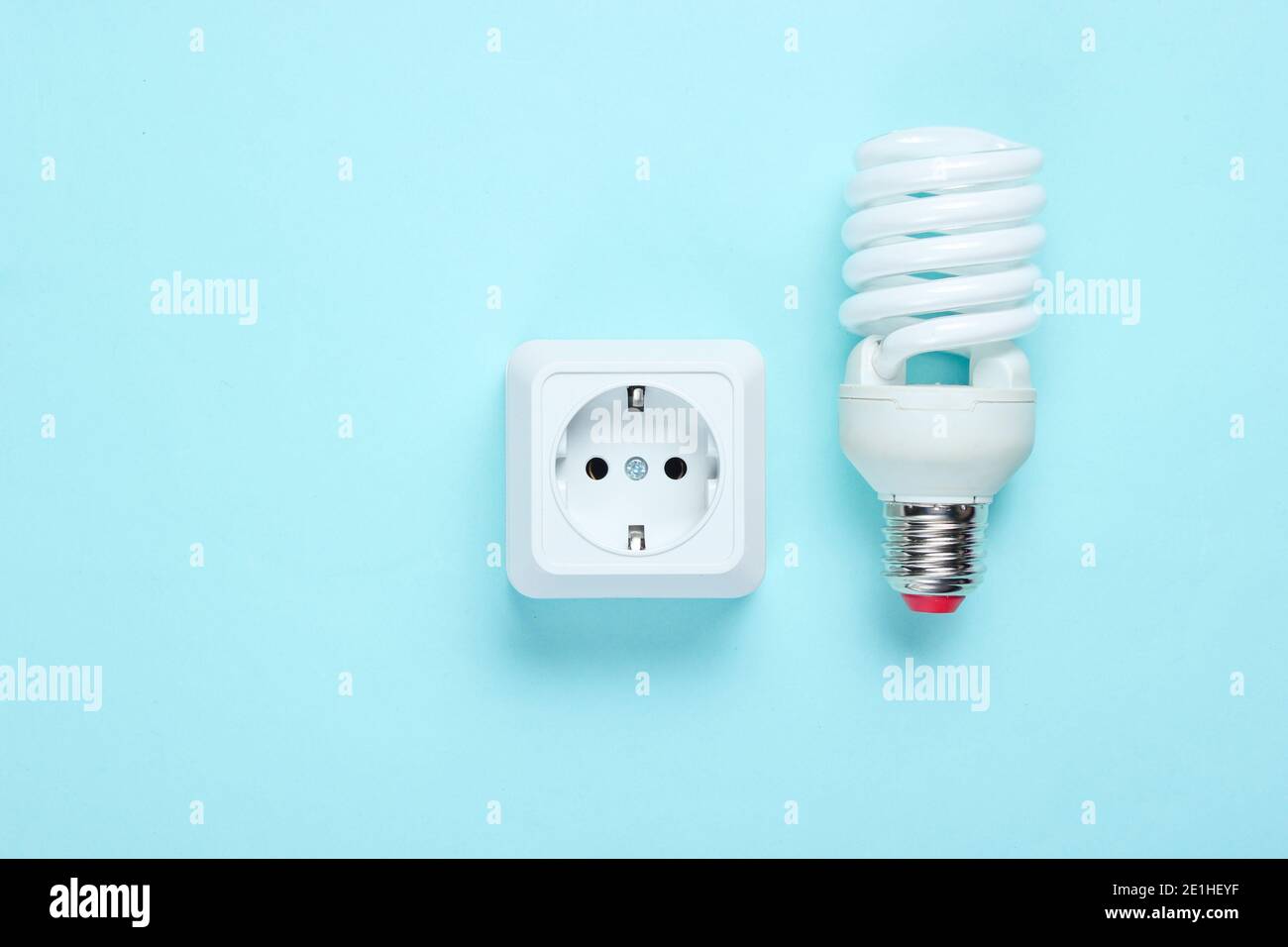 White plastic power socket and spiral light bulb on blue background ...