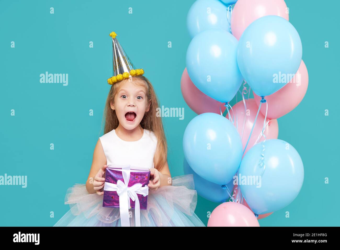 A joyful child girl in an elegant tulle dress and a festive cap holds a ...
