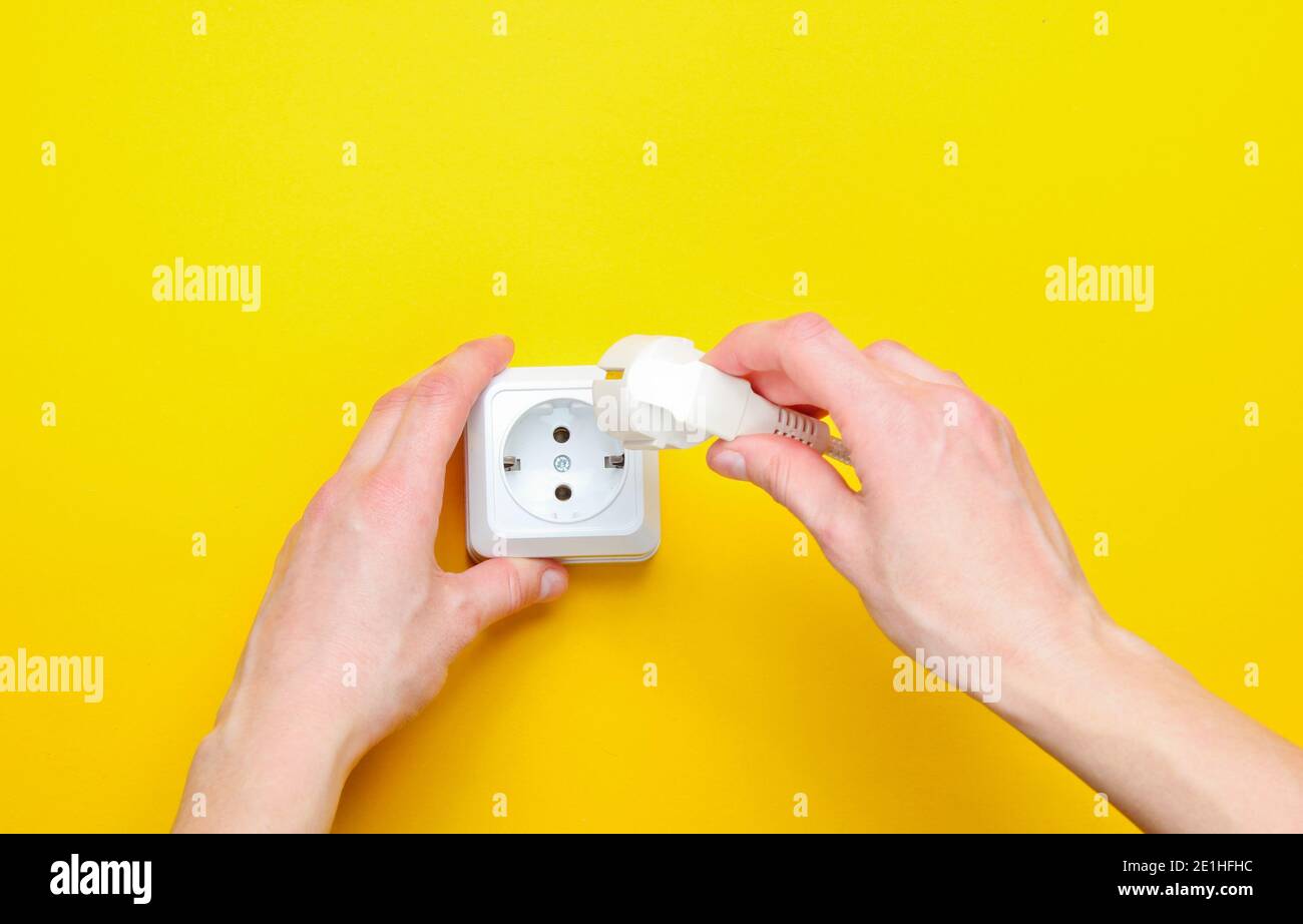 Female hands plug in power plug into electro outlet on yellow ...