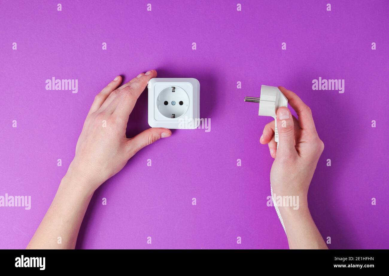 Female hands plug in power plug into electro outlet on purple ...