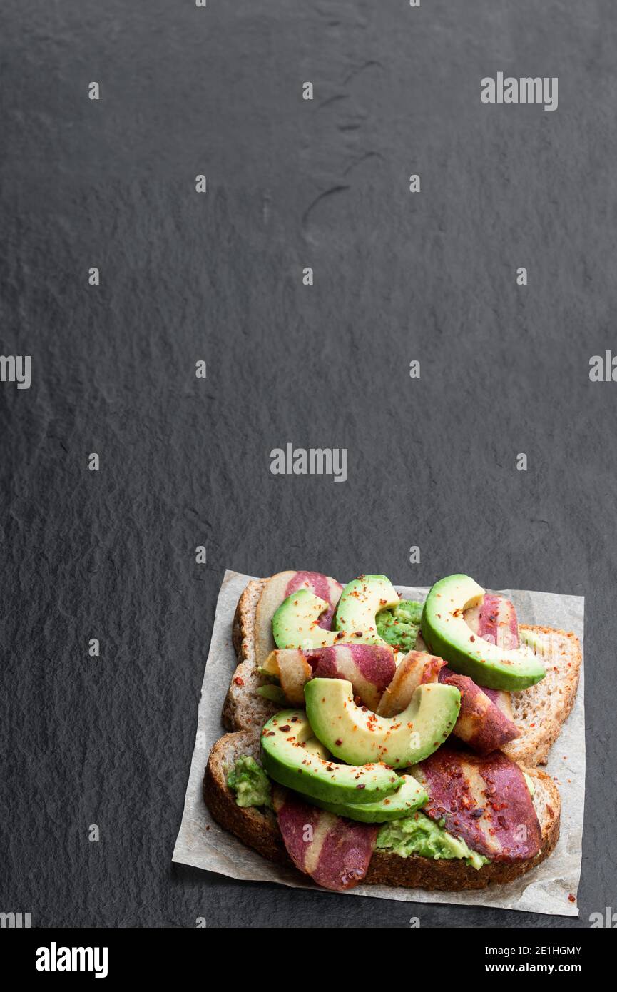 Sandwich with plant-based bacon rashers and avocado on black stone ...