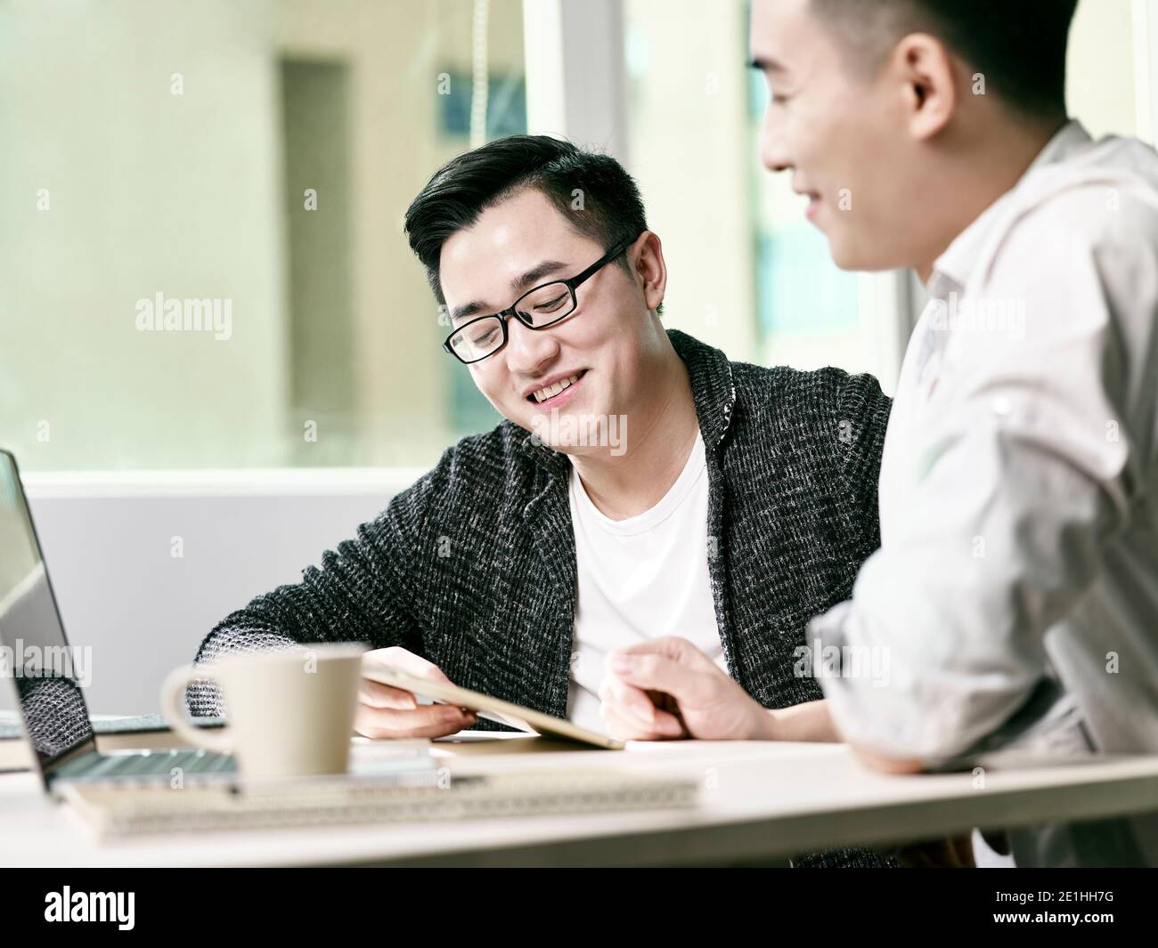 two young asian entrepreneurs discussing business in office using ...