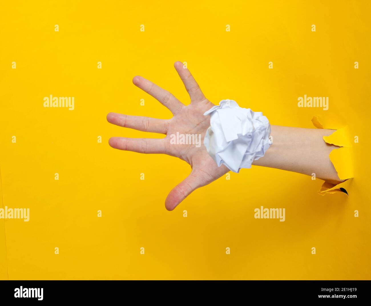 Female hand throws white crumpled ball of paper through the torn yellow ...