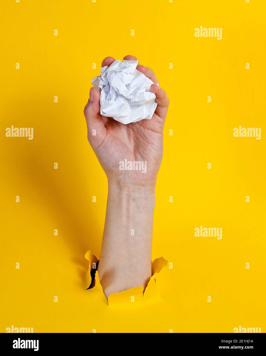 Female hand throws white crumpled ball of paper through the torn yellow ...