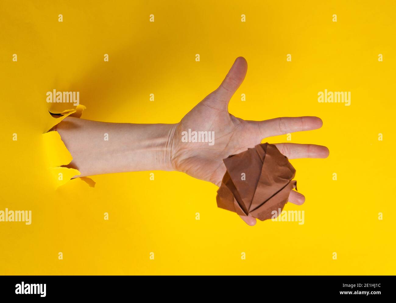 Female hand throws brown crumpled ball of paper through the torn yellow ...