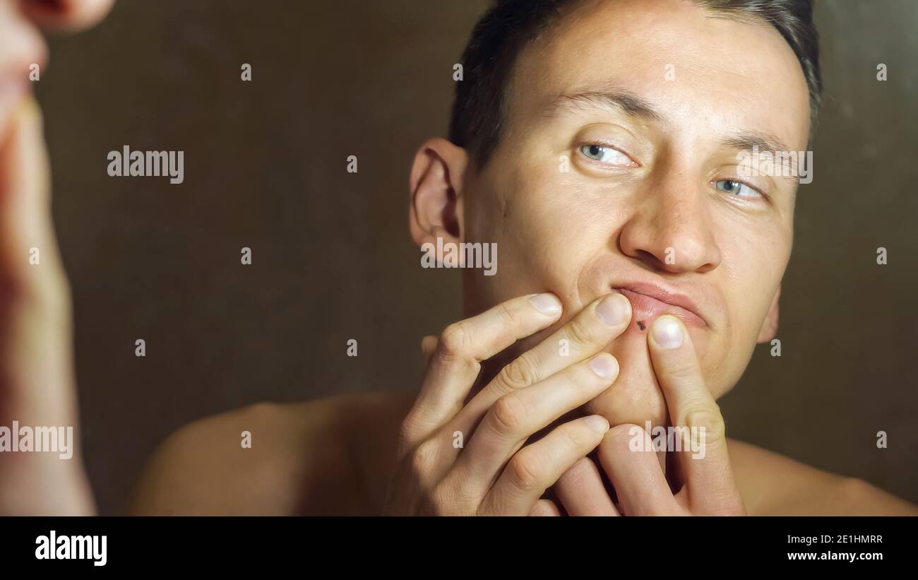 Man with grey eyes looks carefully at mirror reflection of face and ...