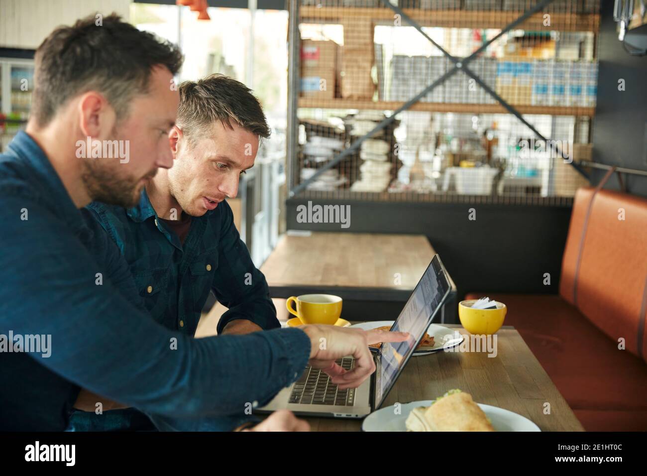 Two men seated in a cafe using a laptop sharing a screen Stock Photo ...