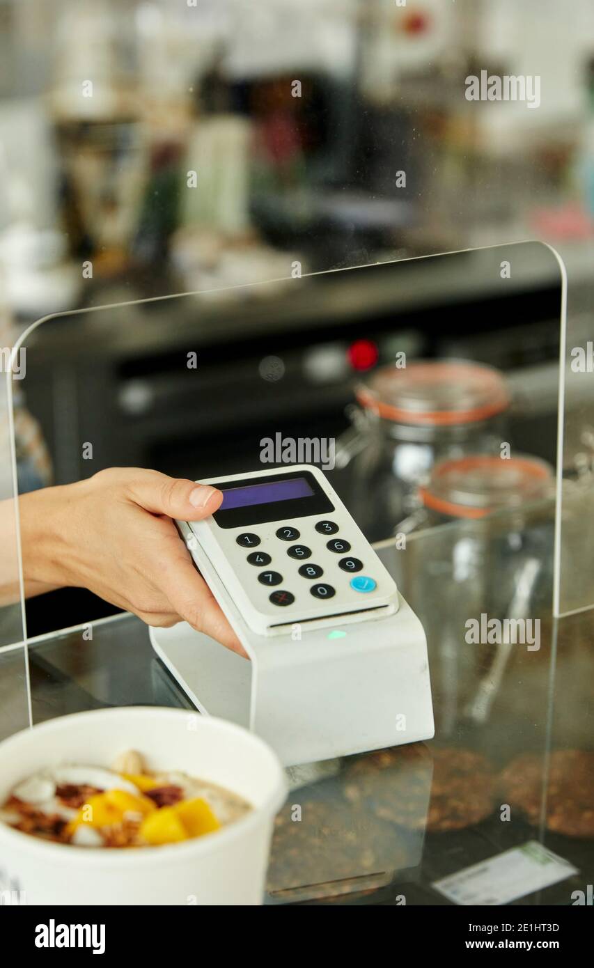 Woman in a face mask behind cafe counter with safety screen, offering a ...