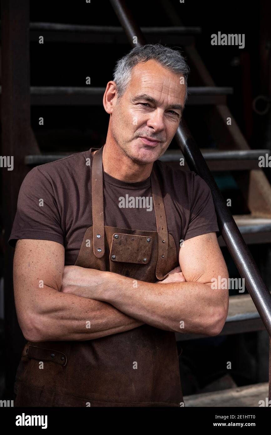 Portrait of male barista with short grey hair, wearing brown apron ...