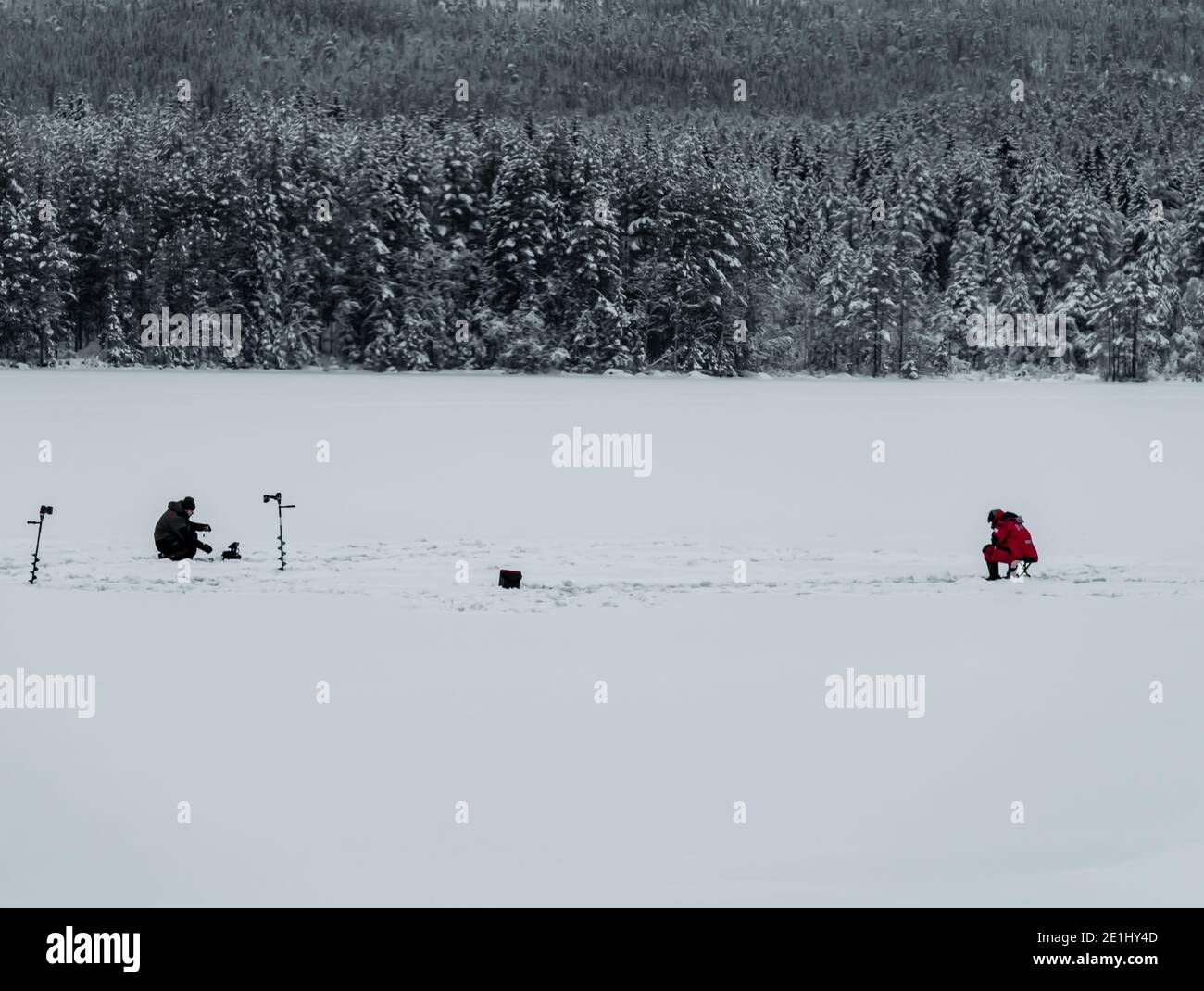 Two men fishing from the ice of a frozen lake covered in deep snow ...