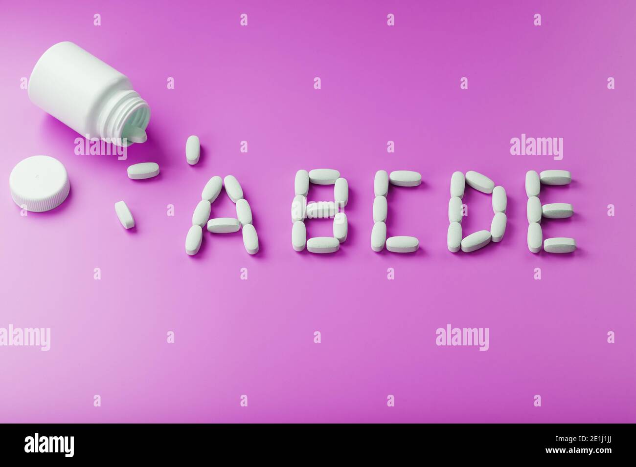 Multivitamins A B C D E in capsules from a jar on a pink background ...