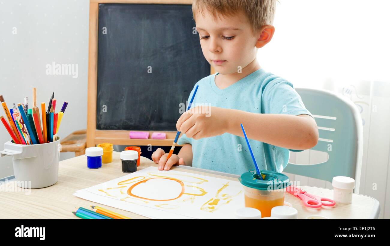 Portrait of cute boy pouring drawing brush in colorful paint and making ...