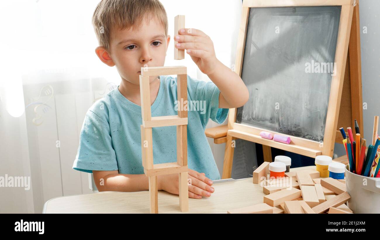 Happy smiling boy building tower with wooden blocks and bricks on desk ...