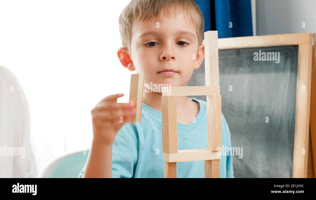 Happy smiling boy putting wooden block on top of high tower made of toy ...