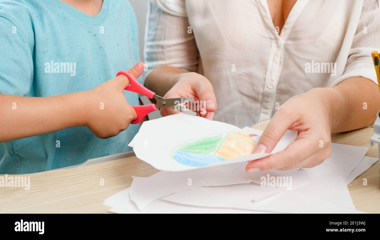 Little boy cutting out drawn picture on paper with scissors. Mother ...