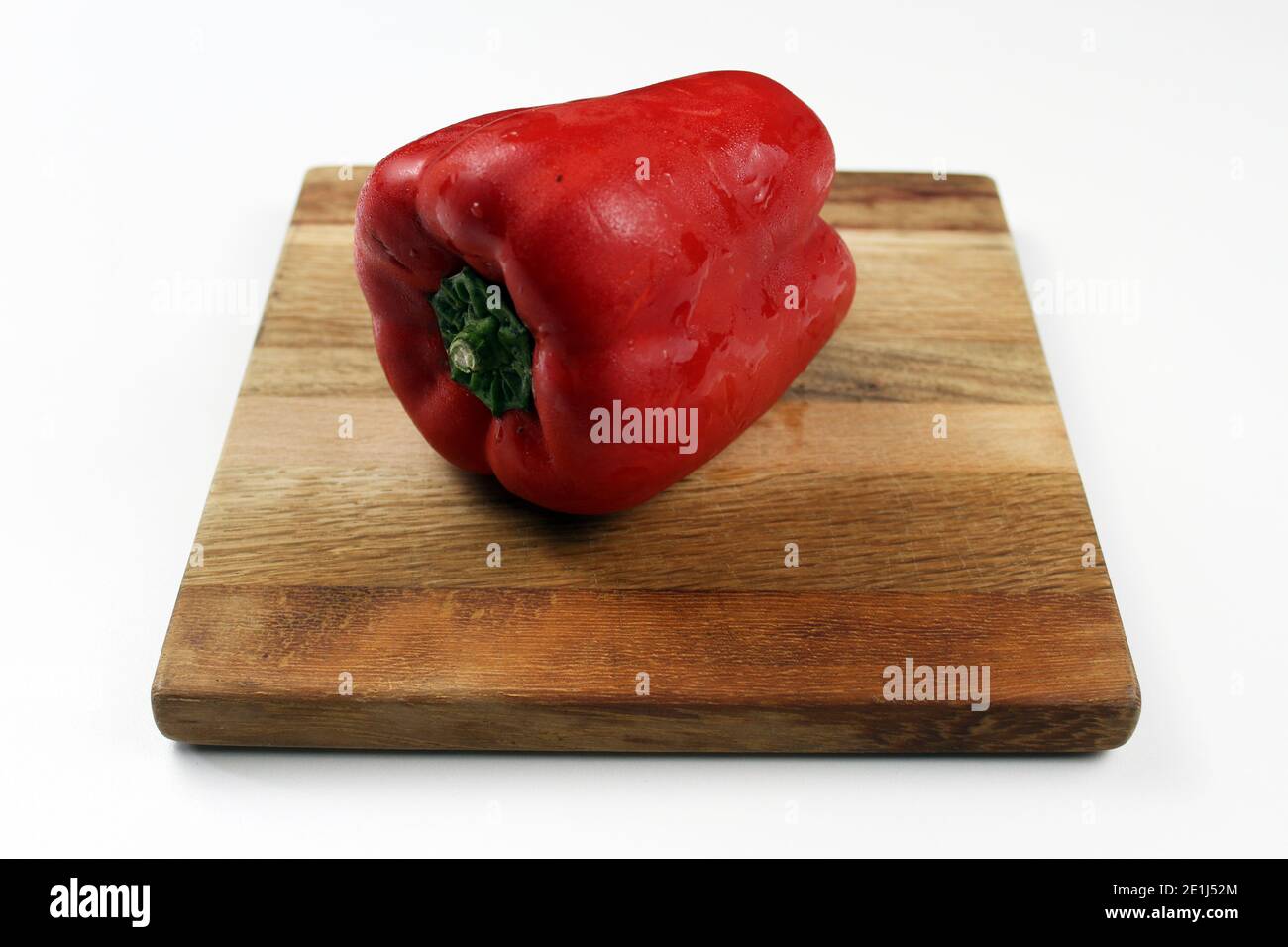 A red pepper on a wooden chopping board against a plain white ...