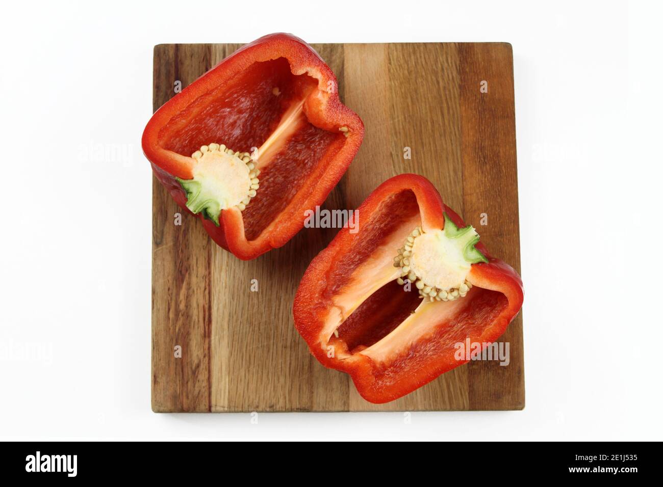 A red pepper on a wooden chopping board against a plain white ...