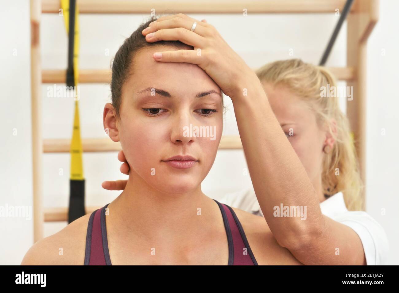 Young physiotherapist exercising with her female patient, fixing head ...