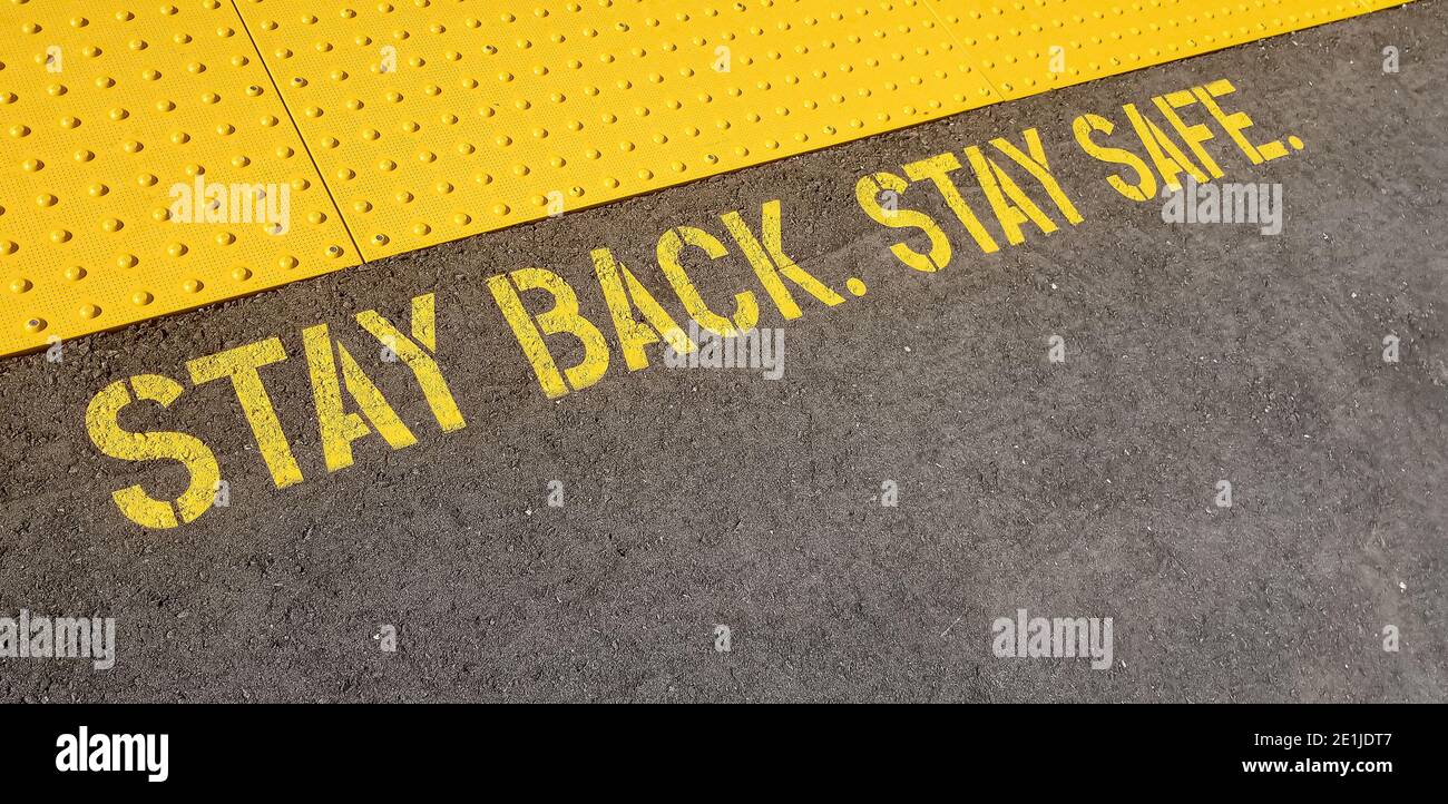 yellow sign at train station asking people to stay back, stay safe, on ...