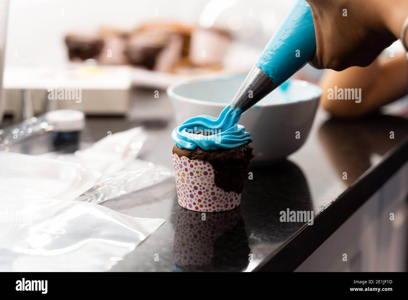 woman adding blue frosting to chocalate cupcake in messy kitchen Stock ...