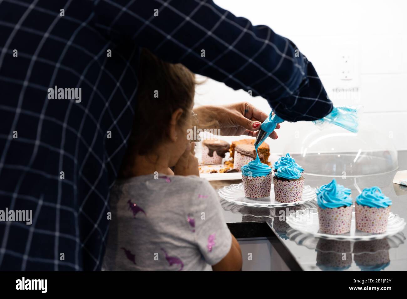 woman adding blue frosting to chocalate cupcakes in messy kitchen ...