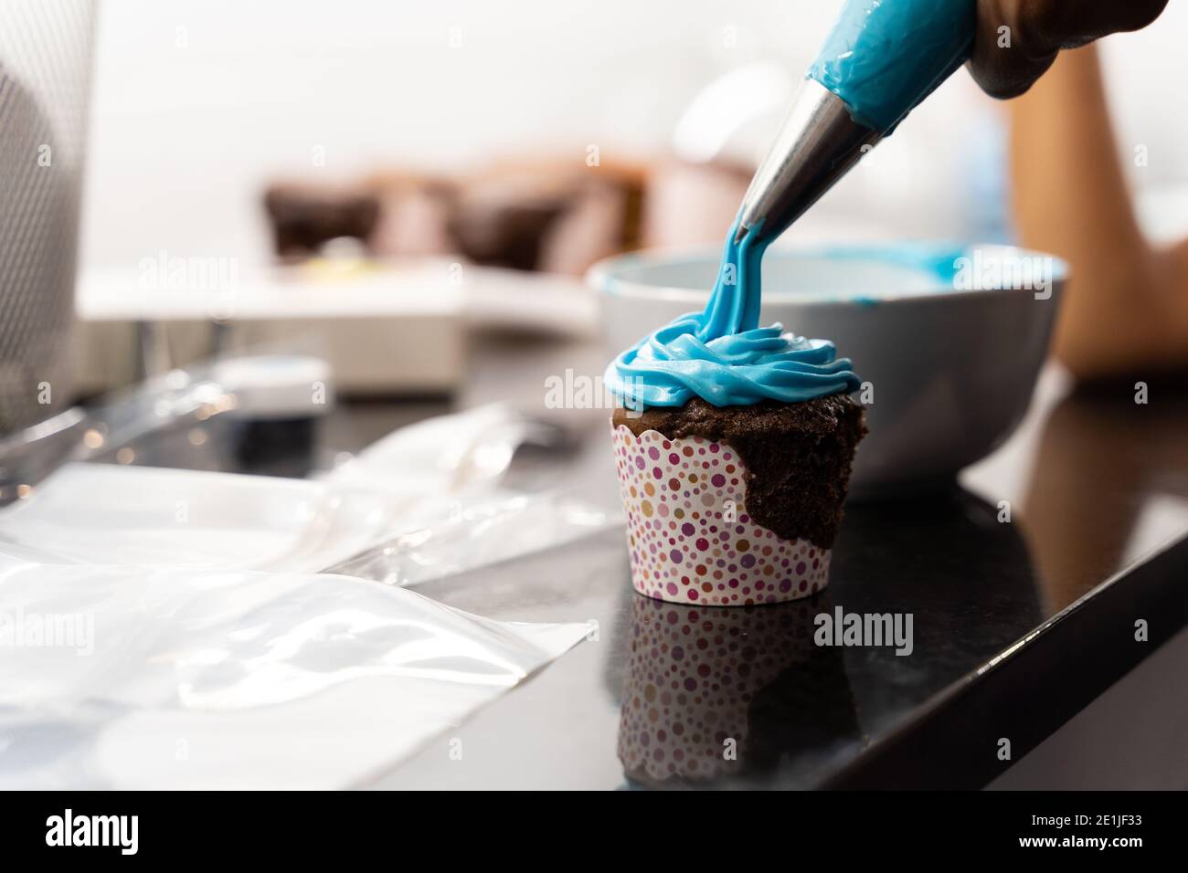 woman adding blue frosting to chocalate cupcake in messy kitchen Stock ...