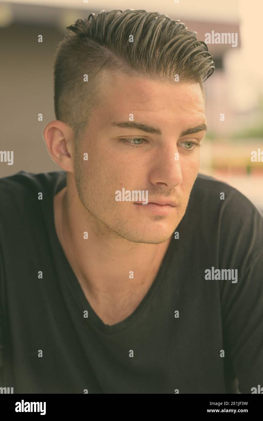 Young handsome man looking down while thinking outside the coffee shop ...