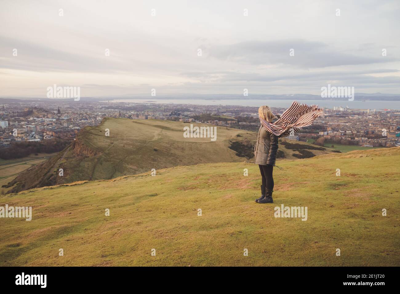 A young woman looks out to the city of Edinburgh, Scotland on a windy ...