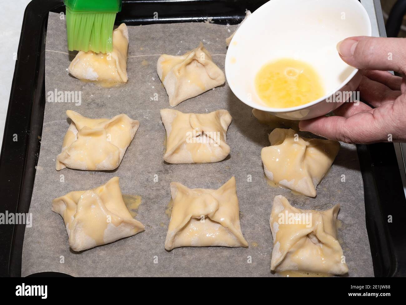 Smearing egg yolk on puff pastry envelopes before baking in the oven ...
