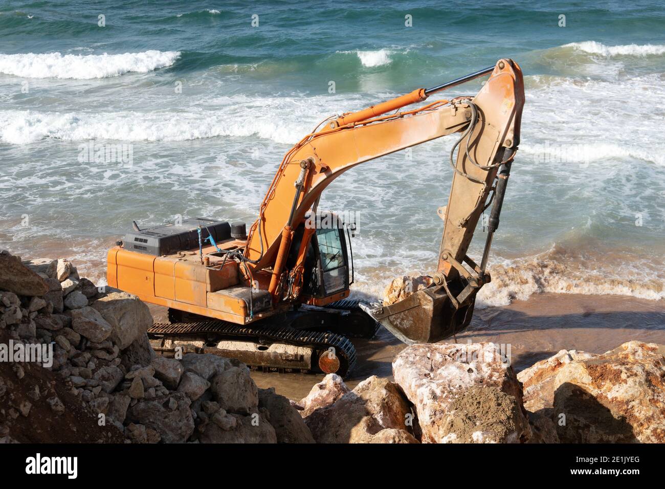 Yellow excavator works on the sea beach with waves on the background in ...