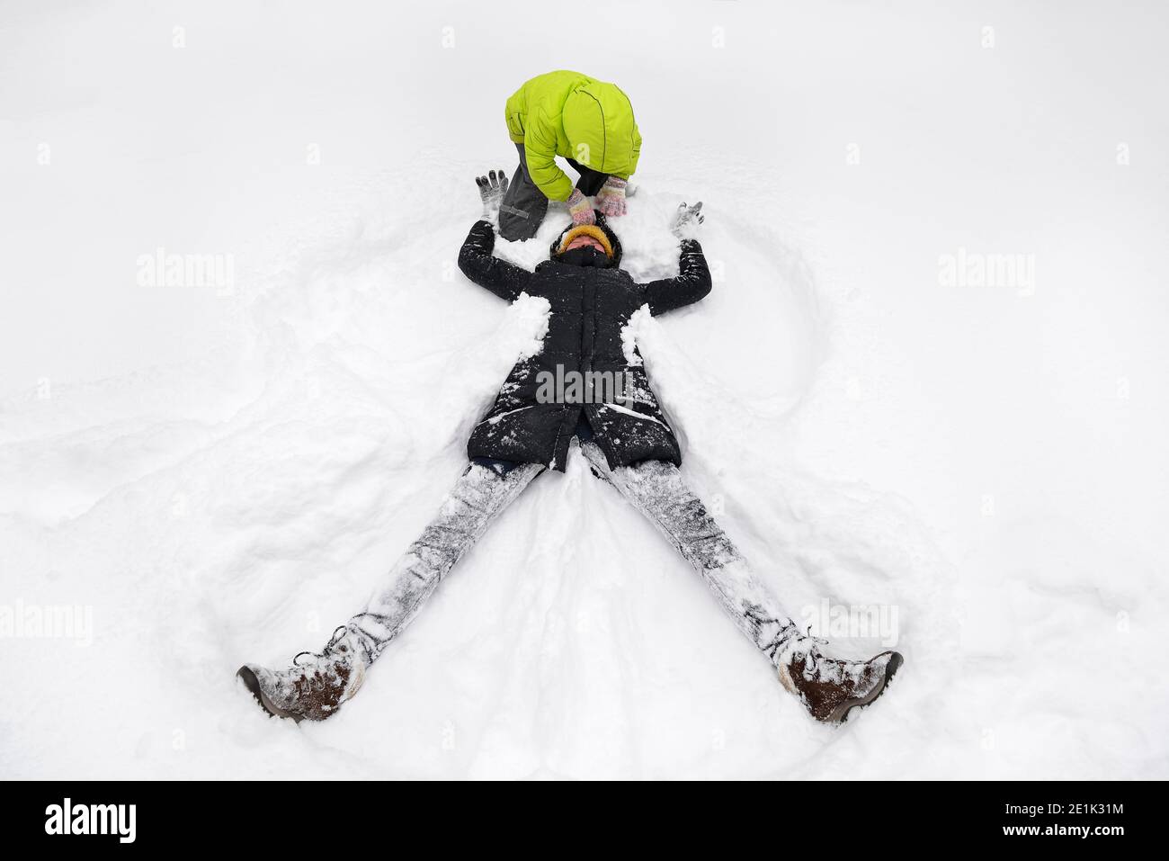 A young woman and her child girl making a snow angel in white deep snow ...