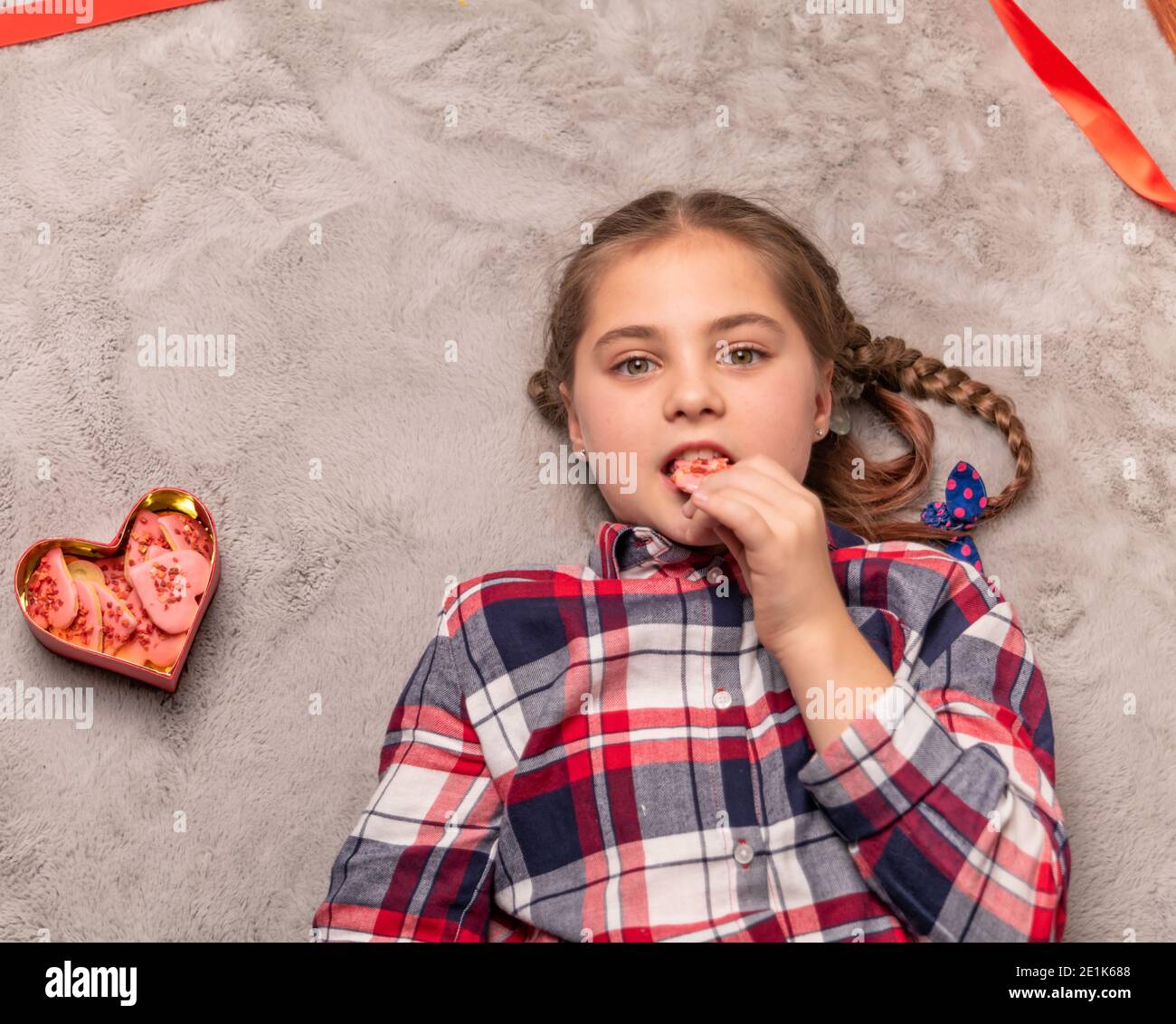 Beautiful girl with pigtails eating cake shape of heart on a grey ...