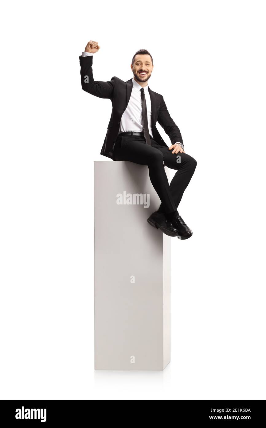 Businessman sitting on a tall white column and gesturing win isolated ...