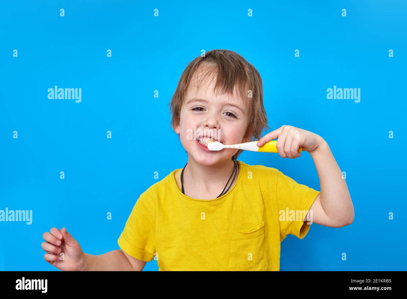 Smiling handsome little boy is brushing his teeth with brush on blue ...
