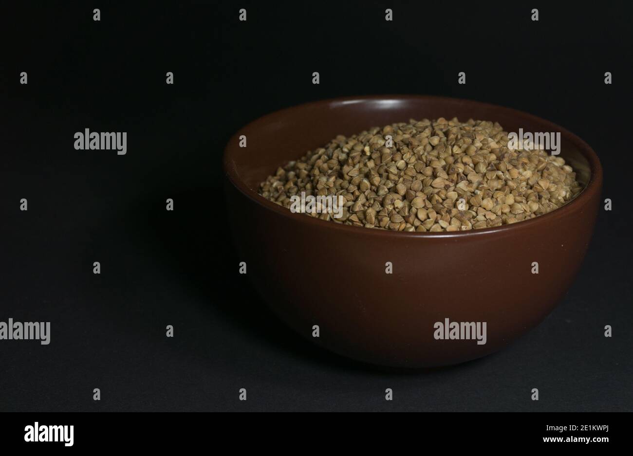 Brown uncooked buckwheat in a bowl with scattered grains nearby on ...