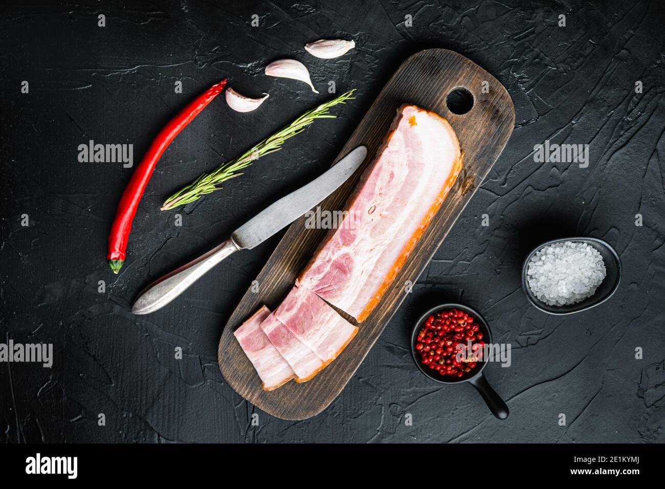 Bacon pancetta cut and sliced with herbs on black background, top view ...