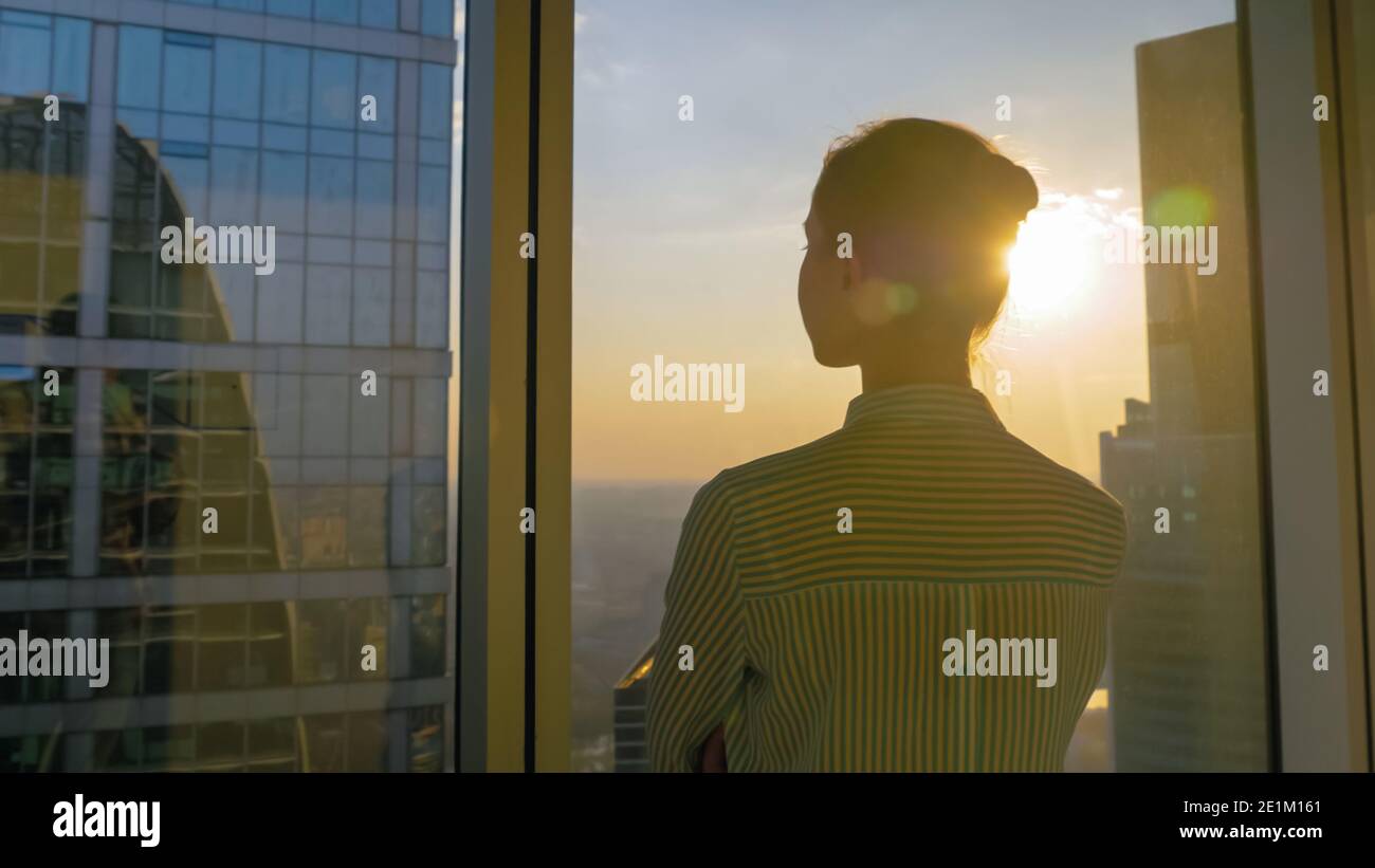 Back view of woman looking at cityscape through glass window of ...