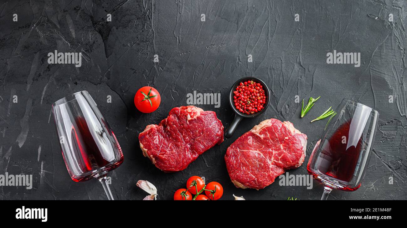 Raw ramp beef cuts with herbs and red wine glasses over black textured ...