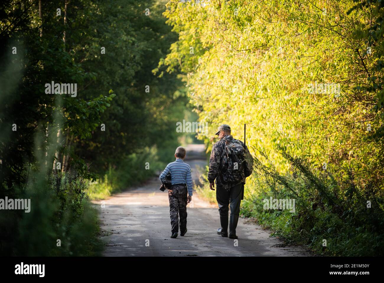 Hunters with hunting equipment going away through rural forest at ...