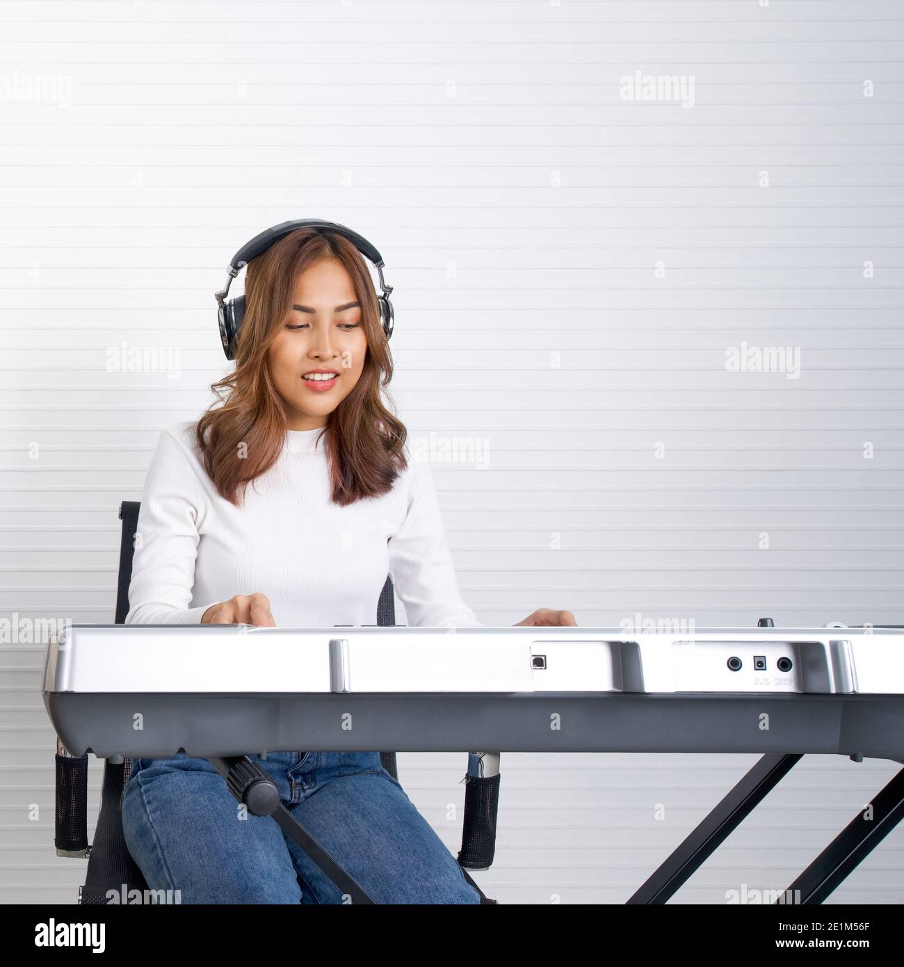 Young asian woman playing an electric keyboard in front of white walls ...