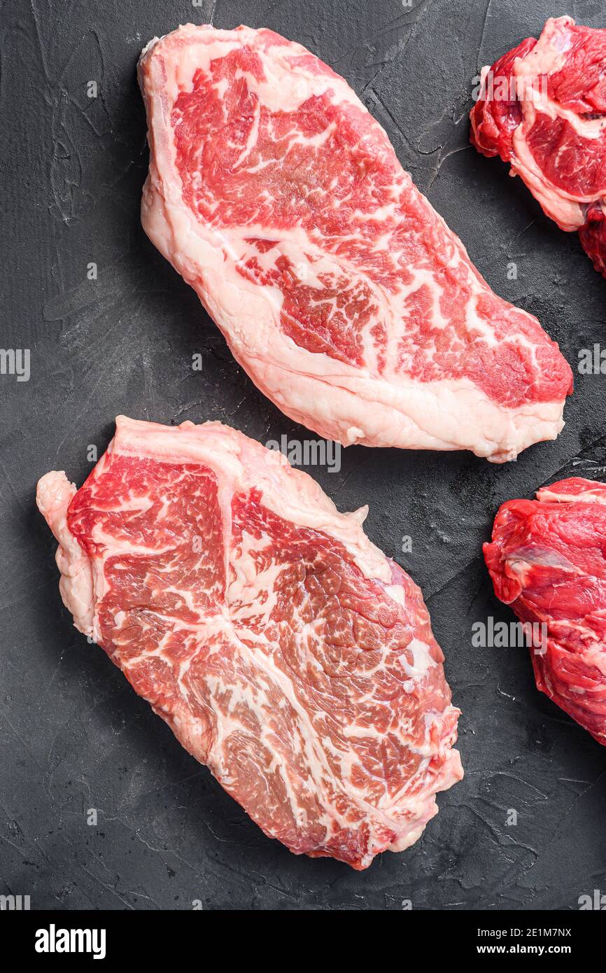 Two raw organic top blade beef steaks, side view on black textured ...