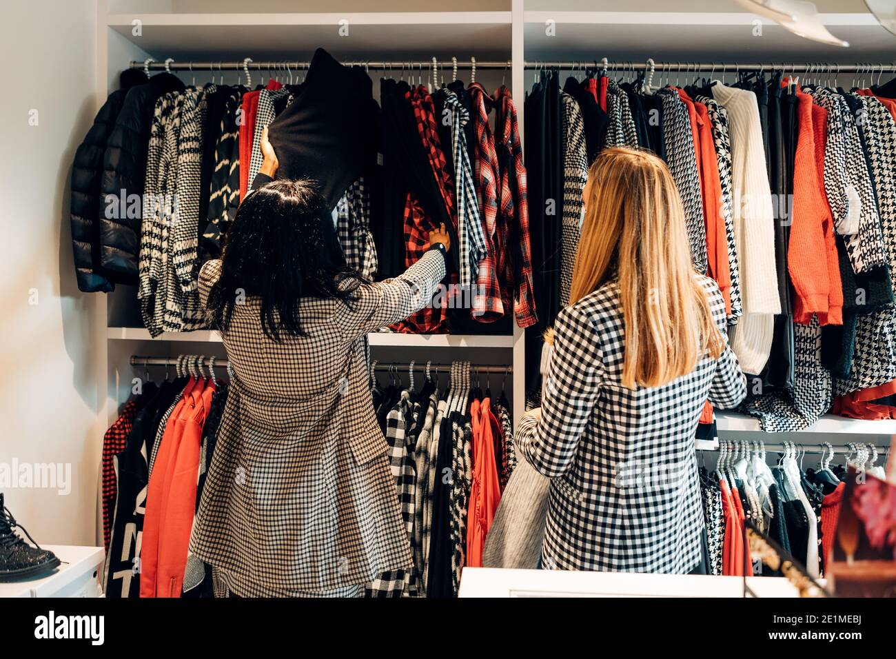 back view of two multi ethnic women standing indoor in a fashion shop ...