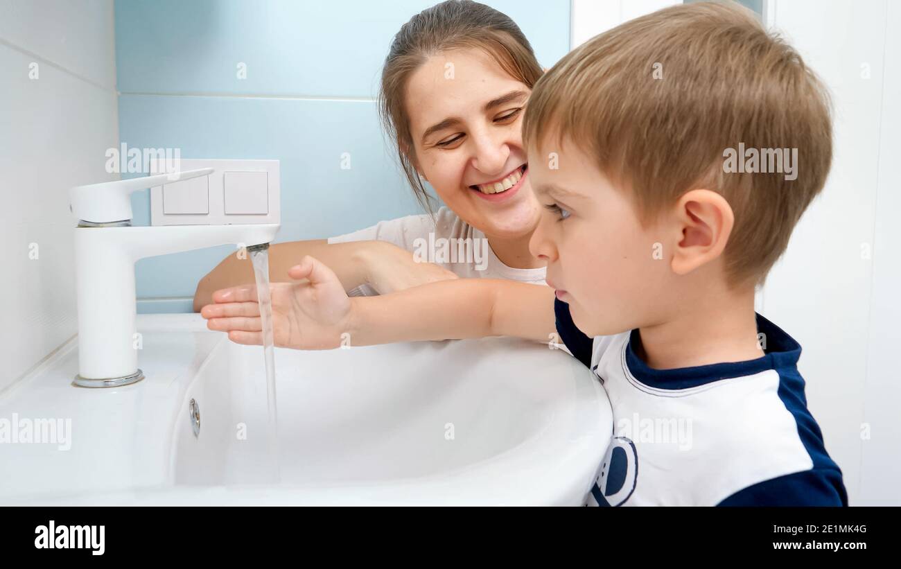 Little boy with mother washing his mouth and face with water and wiping ...