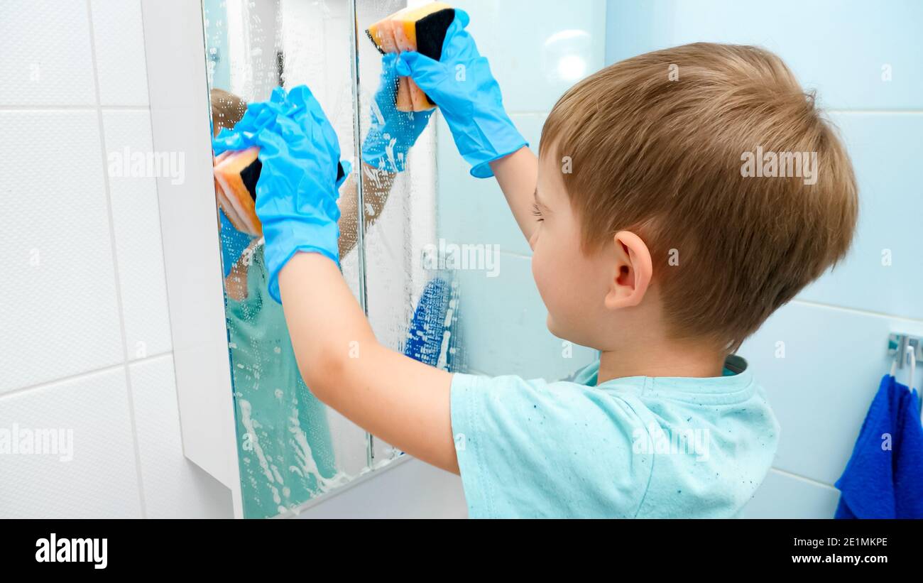 Funny smiling toddler boy washing bathroom mirror with chemical ...